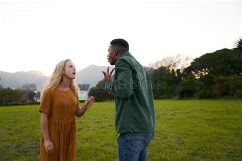 Young Multiracial Couple Face To Face Arguing And Gesturing In Field