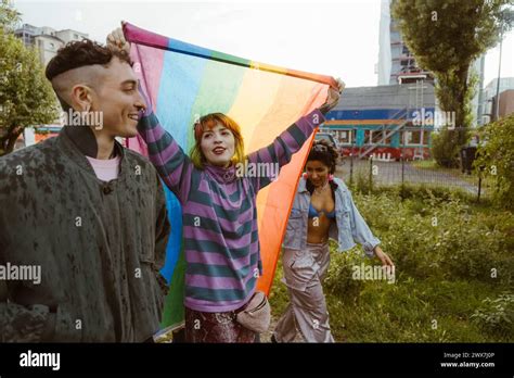 Woman Holding Lgbt Flag While Walking With Non Binary Friends At Park Woman Holding Lgbt Flag While Walking With Non Binary Friends At Park