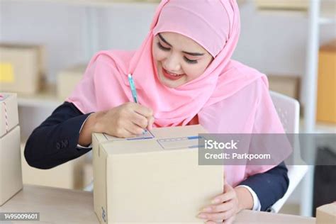 ผู้หญิงเอเชียที่ยิ้มแย้มแจ่มใสในชุดสูทมุสลิมนั่งและทํางานกับการจัดส่ง