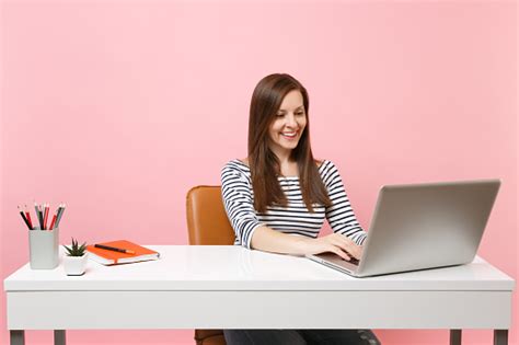 파스텔 핑크 배경에 고립 된 Pc 노트북으로 사무실에 앉아 하는 동안 프로젝트에서 작업 하는 캐주얼 옷에 젊은 웃는 여자 성과 비즈니스 경력 개념입니다 광고에 대 한 공간을