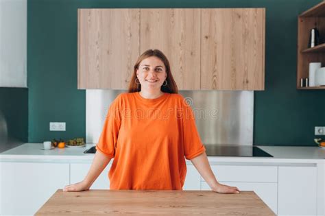 Portrait Of Smiling Young Housewife Standing Near Counter In Modern