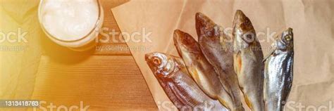 어둡거나 밝은 거품이 나는 맥주 1잔과 소금에 절인 육포 생선 카스피 바퀴벌레 가 수제 종이에 갈색 보드 나무 테이블에 놓여