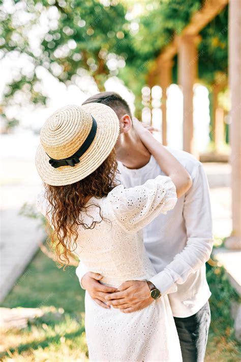 Premium Photo Man Kisses Woman In A Straw Hat Hugging Her Waist In