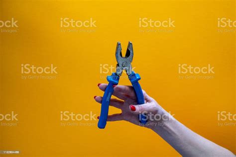 젊은 여자의 손은 파란색 손잡이와 금속 플라이어를 보유 하 고 소녀는 노란색 배경에 근접 한 빨간 매니큐어를가지고 있습니다