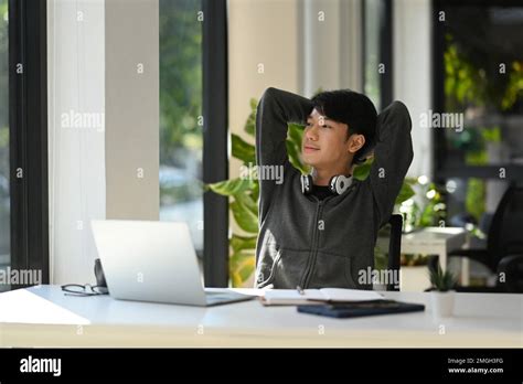 Relaxed Young Asian Man Worker Sitting Back In Office Chair With Hands