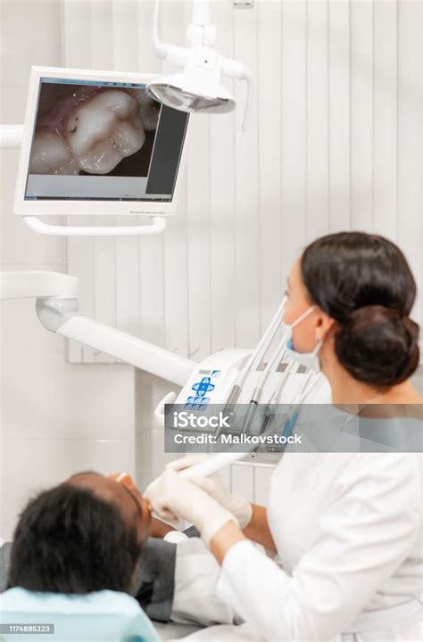 치과 매크로 카메라로 검사하고 모니터에 결과를 표시합니다 치과 진료소에서 근관을 치료하는 젊은 여성 치과 의사 열린 입을 가진