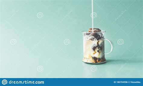 Milk Or Cream Is Poured Into A Glass Cup With Iced Coffee At Pale Blue