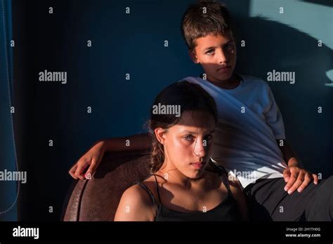 Portrait Of Brother And Sister Sitting Inside Looking At Camera With Serious Expression Source