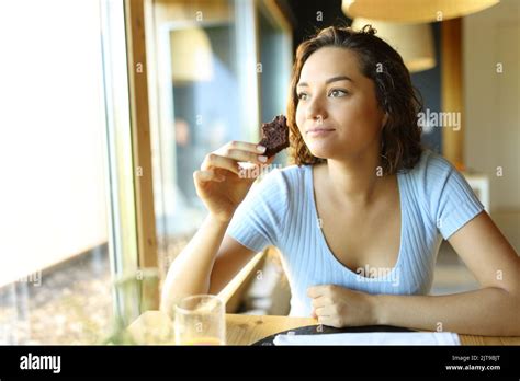 Woman Holding And Eating A Chocolate Cupcake Sitting In A Restaurant