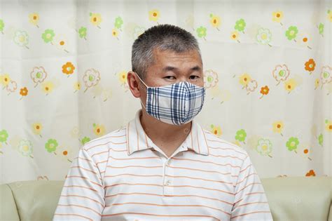 Vista frontal do homem asiático de meia idade sentado no sofá usando