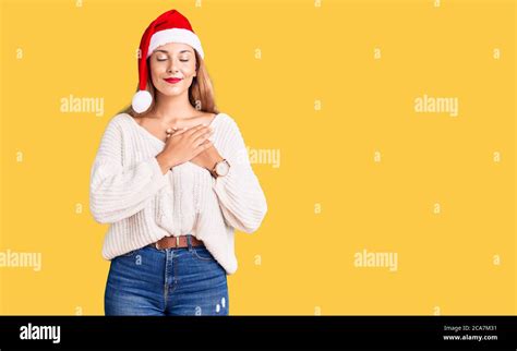 Beautiful Young Woman Wearing Christmas Hat Smiling With Hands On Chest