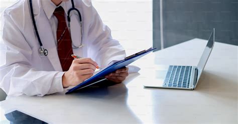 의사는 병원에서 환자 정보를 기록하면서 노트북으로 작업하고 있습니다 사진 Unsplash의 기술 이미지