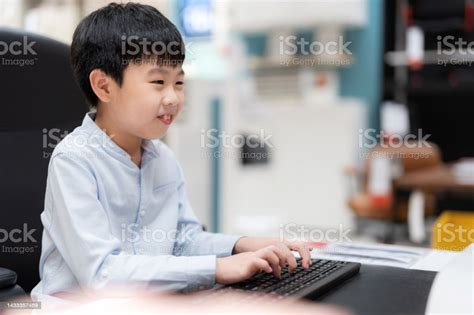 방에서 컴퓨터를 사용하여 셔츠를 입은 젊은 아시아 소년 키보드를 입력하고 미소로 모니터를보고 컴퓨터 게임을하는 아이의 초상화