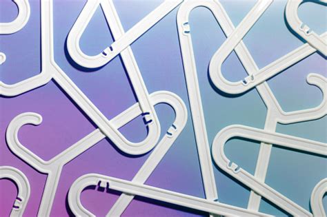 보라색과 파란색 색조의 네온 그라데이션 배경에 추상적인 최소 패턴으로 흰색 플라스틱 옷걸이 옷장이나 소매점에서 옷을 정리하기 위한 옷걸이 옷걸이 평면도 0명에 대한 스톡