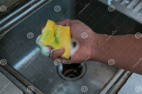 Closeup Of Man Hand Squeezing Dish Soap On Sponge And Washing Dishes In