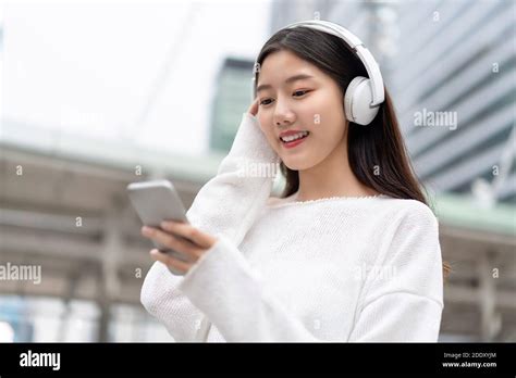 Happy Smiling Asian Girl Wearing Headphones And Looking At Smartphone