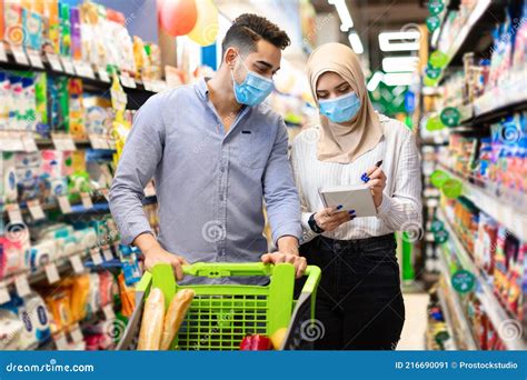 Muslim Couple Taking Notes In List Buying Food In Supermarket Stock