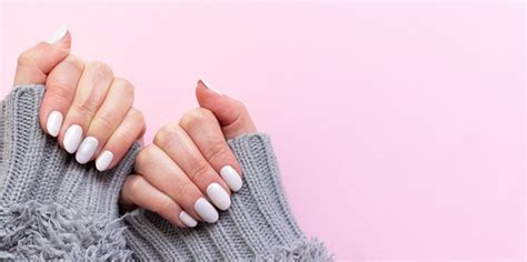 아름다운 매니큐어와 회색 니트 스웨터에 여성의 손 분홍색 종이 배경에 흰색 상아 손톱 복사 공간이있는 템플릿 배너 분홍색 배경에