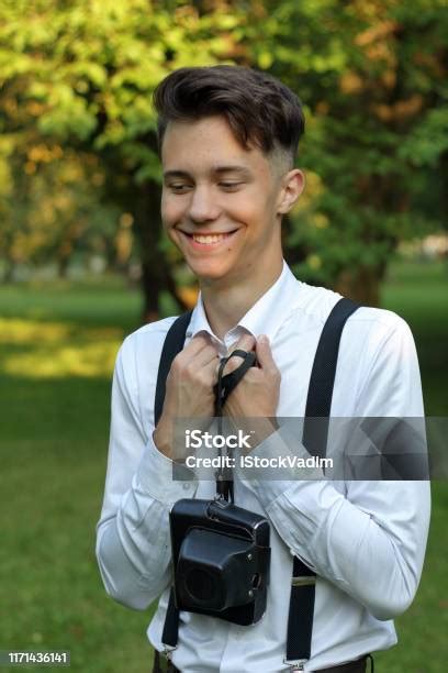 ชายหนุ่มที่แต่งตัวอย่างมีสไตล์โพสท่าในสวนสาธารณะ หัวเราะนํามือของเขาไปที่หน้าอกของเขา ภาพสต็อก