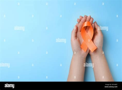 Woman Holding Orange Ribbon On Light Blue Background Top View With