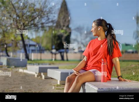 Latin Girl With Wireless Headphones Sitting On A Bench In A Public Park