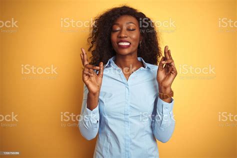 고립 된 노란색 배경 제스처 손가락 위에 우아한 셔츠를 입고 아프리카 계 미국인 사업가는 희망과 눈을 감고 미소를 교차 행운과