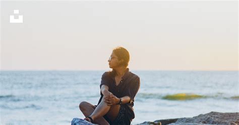Woman In Black Tank Top Sitting On Rock Near Sea During Daytime Photo