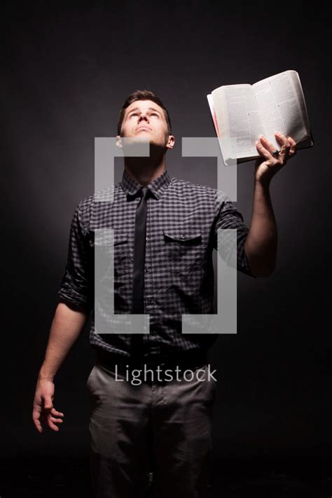 A Man Holding An Open Book In His Hand And Looking Up Into The Sky With