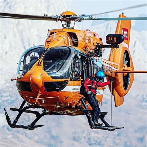 Orange Airbus H145 Helicopter Flying Over Italian Alps
