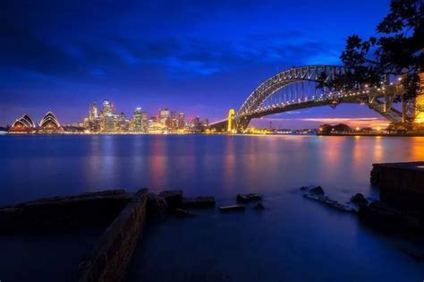 The Sydney Bridge Is Lit Up At Night With Lights Reflecting Off The