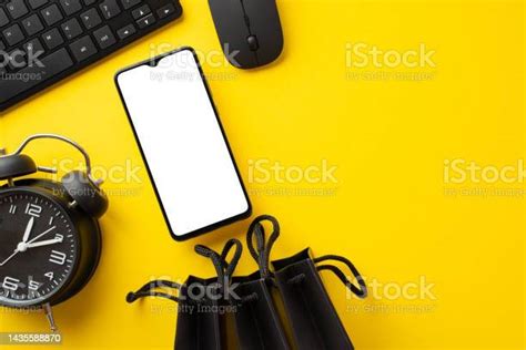 블랙 프라이데이 개념 스마트폰 키보드 컴퓨터 마우스 검은 종이 봉지와 빈 공간이 있는 격리된 노란색 배경에 알람 시계의 상위 뷰