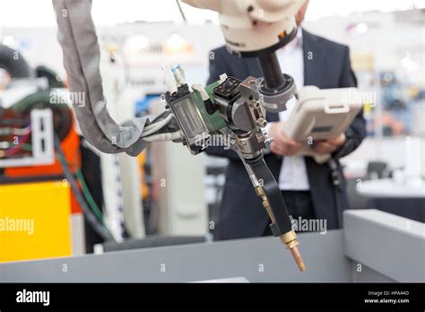 Industrial Welding Robot Arm In The Focus Blurred Operator In The