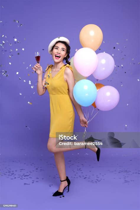 화려한 풍선과 와인 잔을 들고 축하 파티에서 예쁜 젊은 아시아 여성은 그녀의 사방에 떨어지는 색종이와 함께 즐길 수 있습니다 새해 복 많은 새해 또는 생일 전야 개념 축하